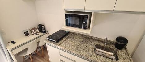 Uma cozinha compacta com micro-ondas, torradeira e cafeteira sobre uma bancada de granito.
