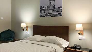 Quarto de hotel com cama, duas luminárias de cabeceira, mesa de cabeceira com telefone, uma cadeira e ar-condicionado fixado na parede.