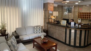 Uma área de recepção de hotel com um balcão curvo, um sofá, uma mesa de centro e um vaso de planta.