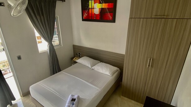 Quarto de hotel com cama, guarda-roupa, escrivaninha e janela com cortinas.