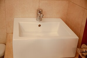 Casa de banho com lavatório branco, torneira e sanita.