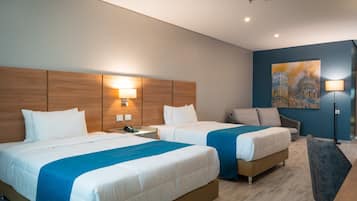 Quarto de hotel com duas camas, uma escrivaninha, uma cadeira e um quadro na parede.