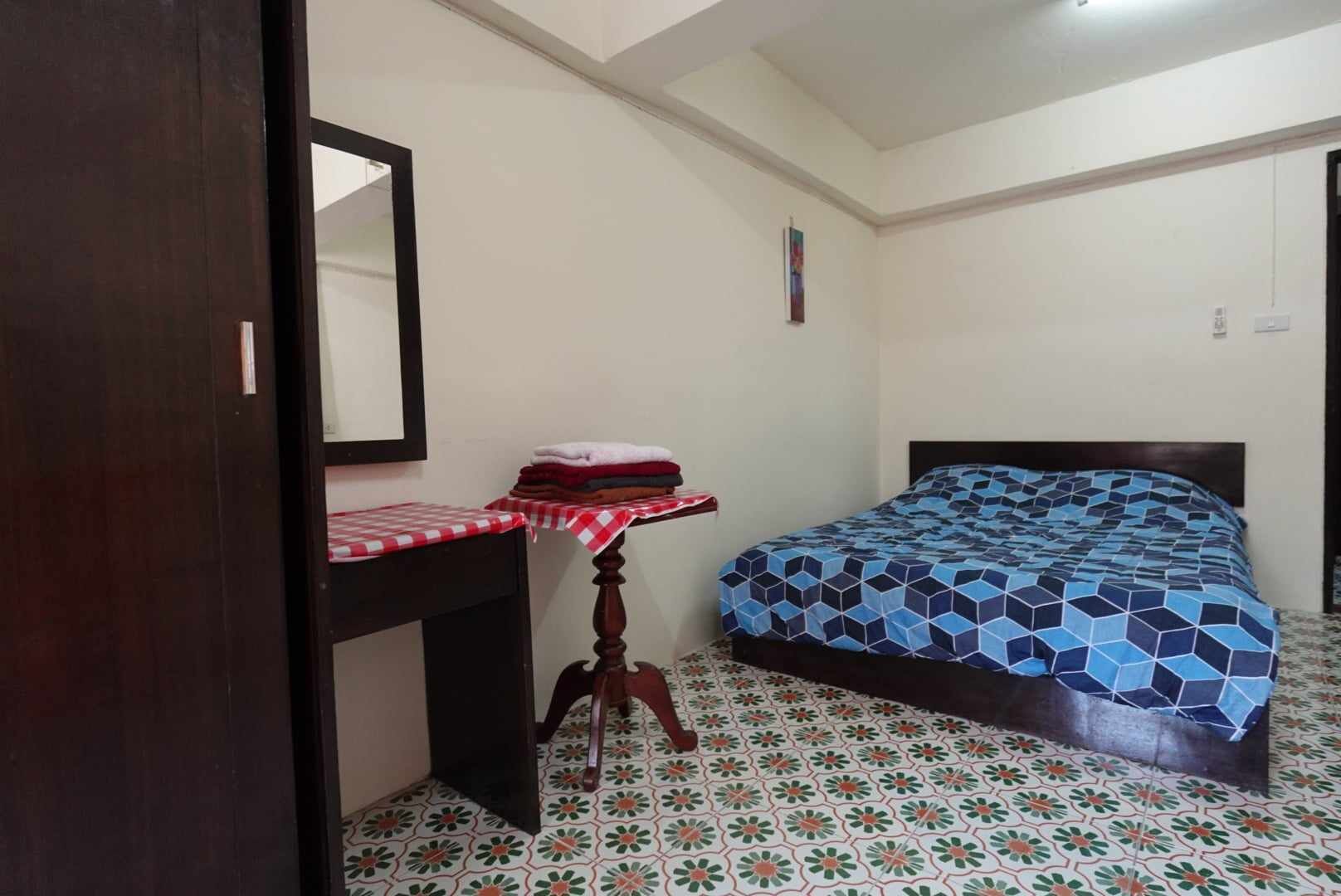 Quarto com cama, uma mesa com toalha xadrez e piso de azulejos.