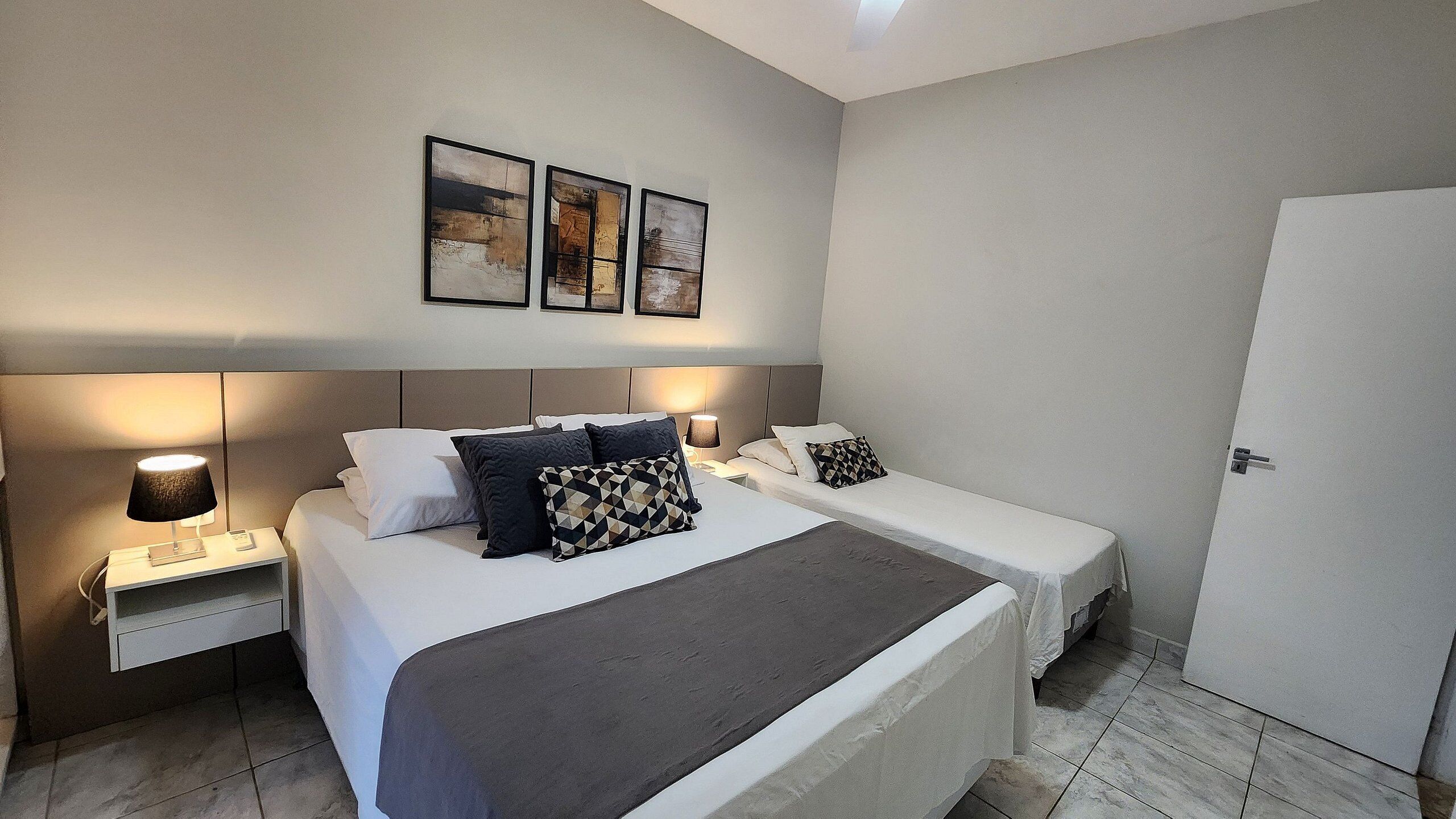 Quarto de hotel com cama, mesas de cabeceira, luminárias e obras de arte na parede.