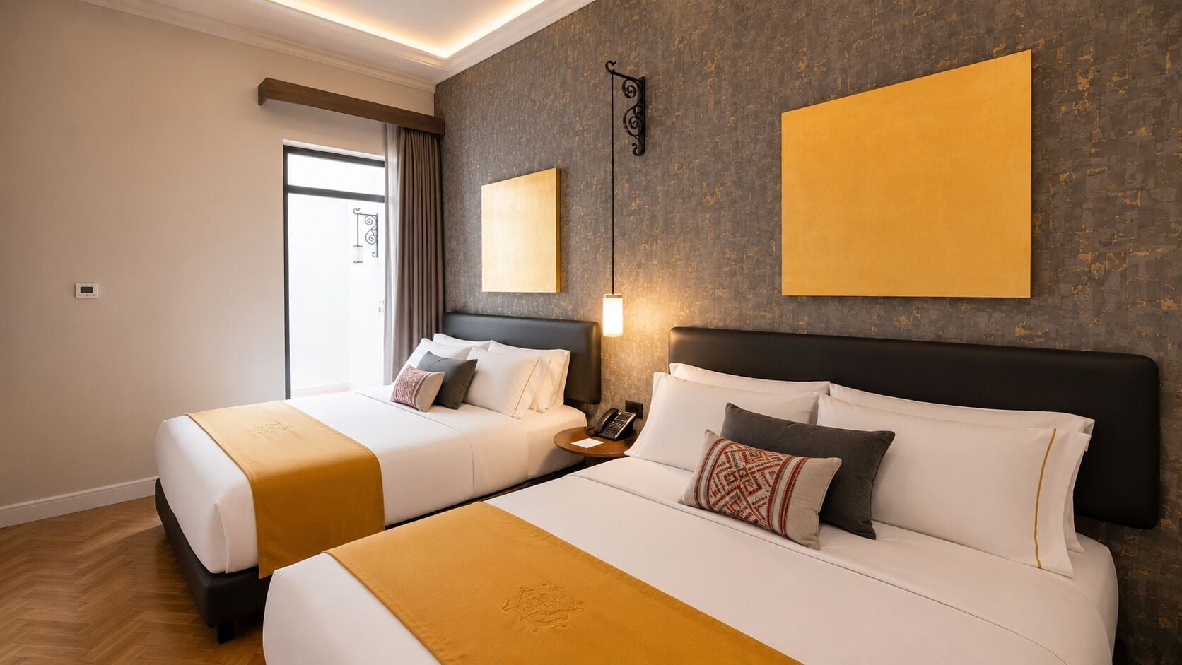 Quarto de hotel com duas camas, uma janela grande, telefone fixado na parede e uma obra de arte na parede.
