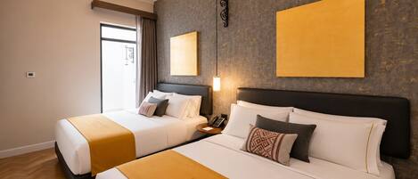 Quarto de hotel com duas camas, uma janela grande, telefone fixado na parede e uma obra de arte na parede.