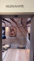 Interior de restaurante com paredes de tijolos aparentes, vigas de madeira e uma mesa de madeira com cadeiras.