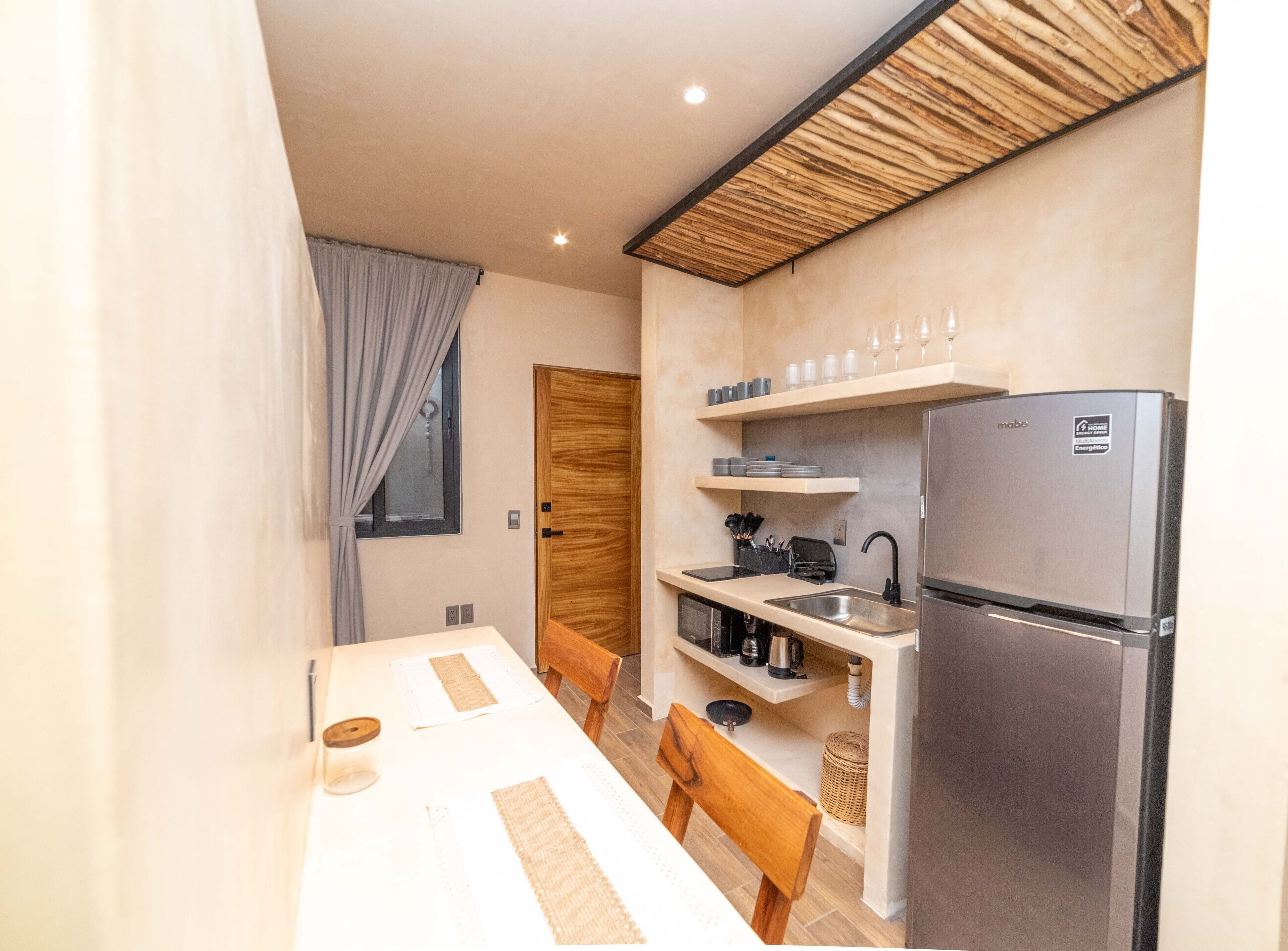 Uma cozinha compacta com frigorífico embutido, armários de madeira e um espaço de refeições com mesa e cadeiras.