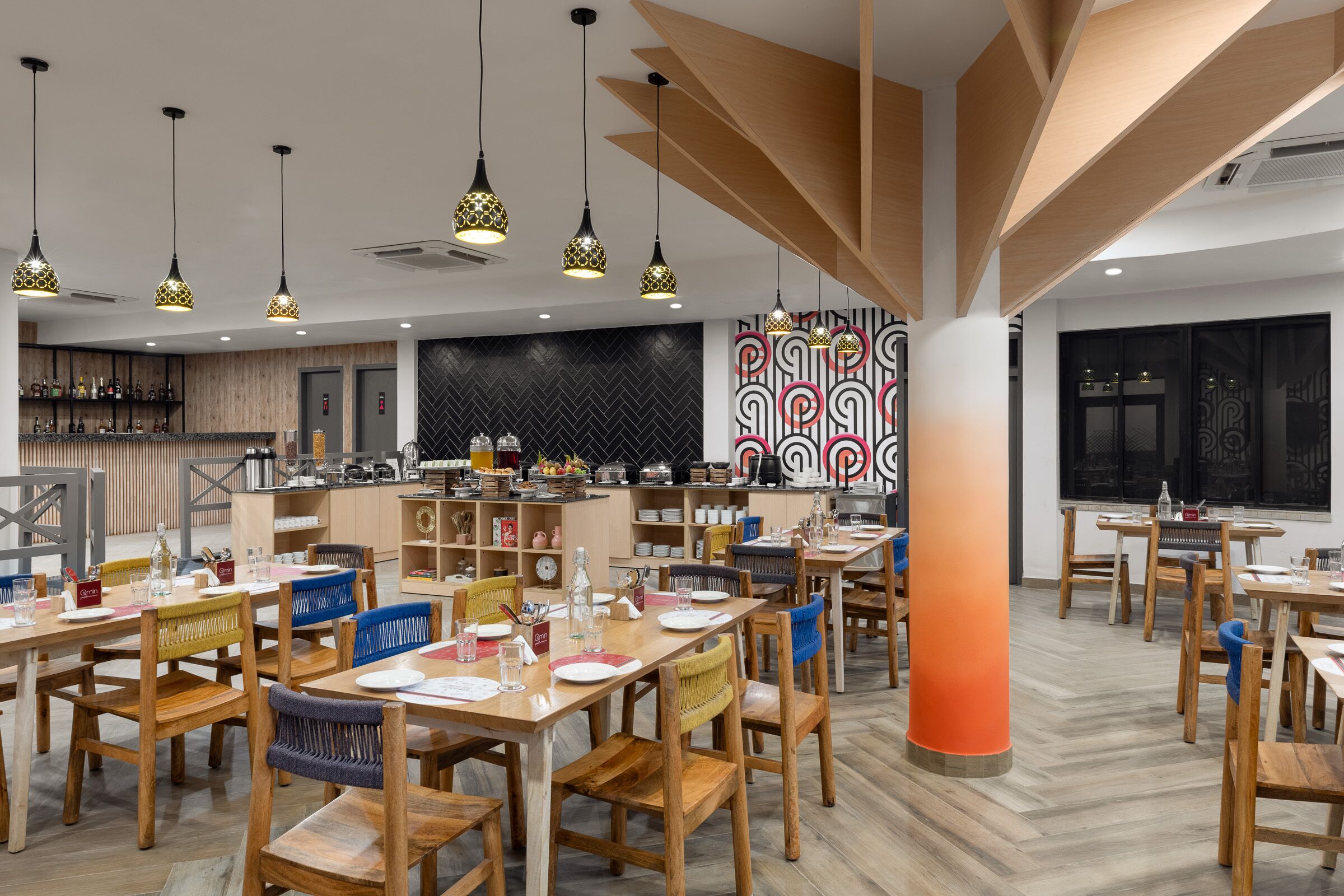 Um restaurante moderno com mesas e cadeiras de madeira, iluminação pendente e parede com padrão losango.