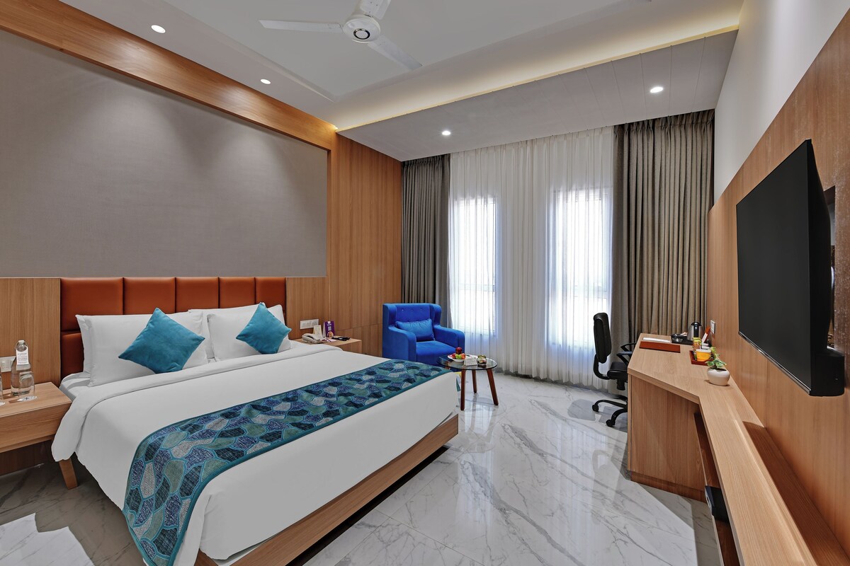 Quarto de hotel moderno com uma cama grande, uma mesa, uma cadeira e uma televisão.