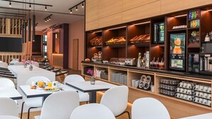 Uma área de café da manhã moderna em hotel, com buffet, assentos e estação de café.