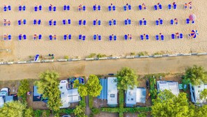 Vista aérea de um camping com várias trailers e barracas, fileiras organizadas de cadeiras de praia e uma área de areia.