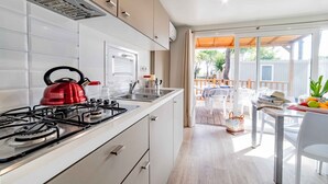 Cozinha moderna com fogão a gás, chaleira e armários brancos. Possui uma área de jantar com mesa e cadeiras, e vista para o exterior.