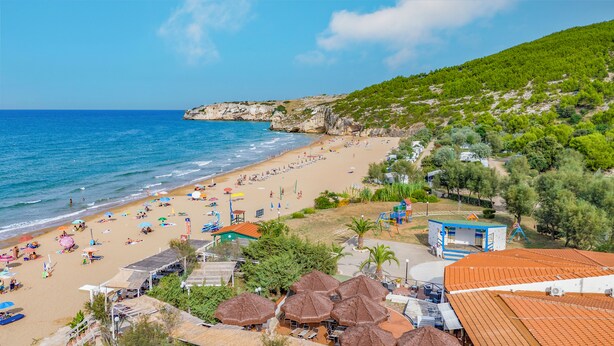 Uma praia com guarda-sóis, espreguiçadeiras e um trecho costeiro rochoso.