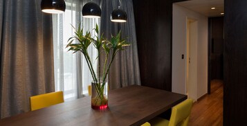 Uma área de refeições com mesa de madeira, cadeiras amarelas, um vaso de vidro com planta e luminárias pendentes pretas.