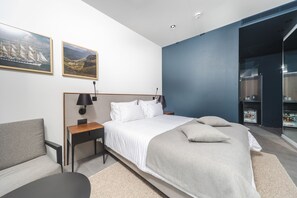 Quarto moderno com uma cama grande, uma mesa de cabeceira, uma escrivaninha e duas fotos emolduradas na parede.