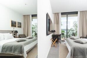 Quarto de hotel com cama, escrivaninha e uma janela grande com cortinas.