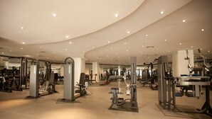 Academia moderna com diversos equipamentos de exercício, teto curvo e iluminação abundante.