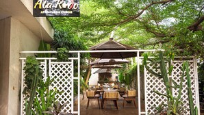 Área de estar coberta ao ar livre, com pérgola, rodeada por vegetação exuberante e plantas em vasos.