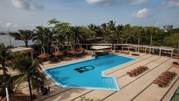 Área de piscina com espreguiçadeiras, guarda-sóis e palmeiras.