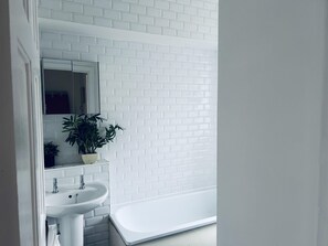 Um banheiro com azulejos brancos tipo metrô, pia branca, espelho e banheira.