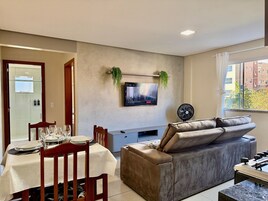Uma sala de estar moderna com área de jantar, televisão de tela plana na parede, sofá e mesa de pebolim.