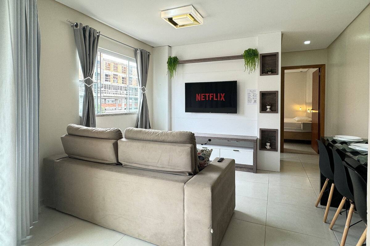Uma sala de estar moderna com um sofá, uma TV na parede e um espaço de jantar com mesa e cadeiras.