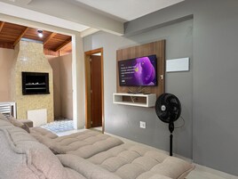 Uma sala de estar moderna com televisão de tela plana na parede, um ventilador de chão e um sofá bege grande.