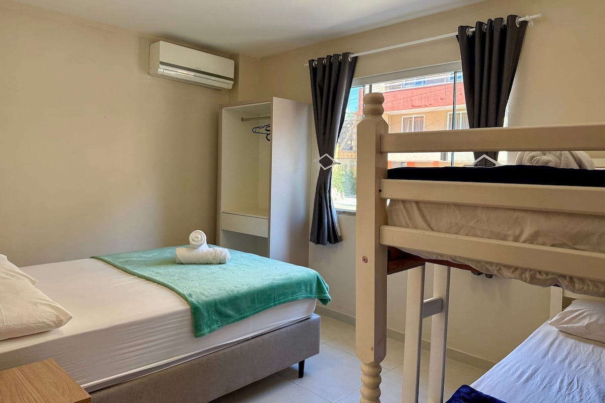 Quarto com cama beliche, uma cama de solteiro, guarda-roupa e ar condicionado.