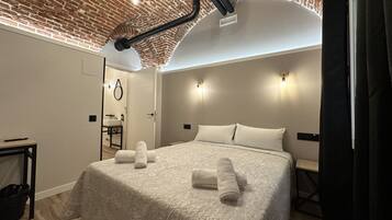Quarto moderno com teto de tijolos, uma cama grande com lençóis brancos e duas luminárias fixadas na parede.