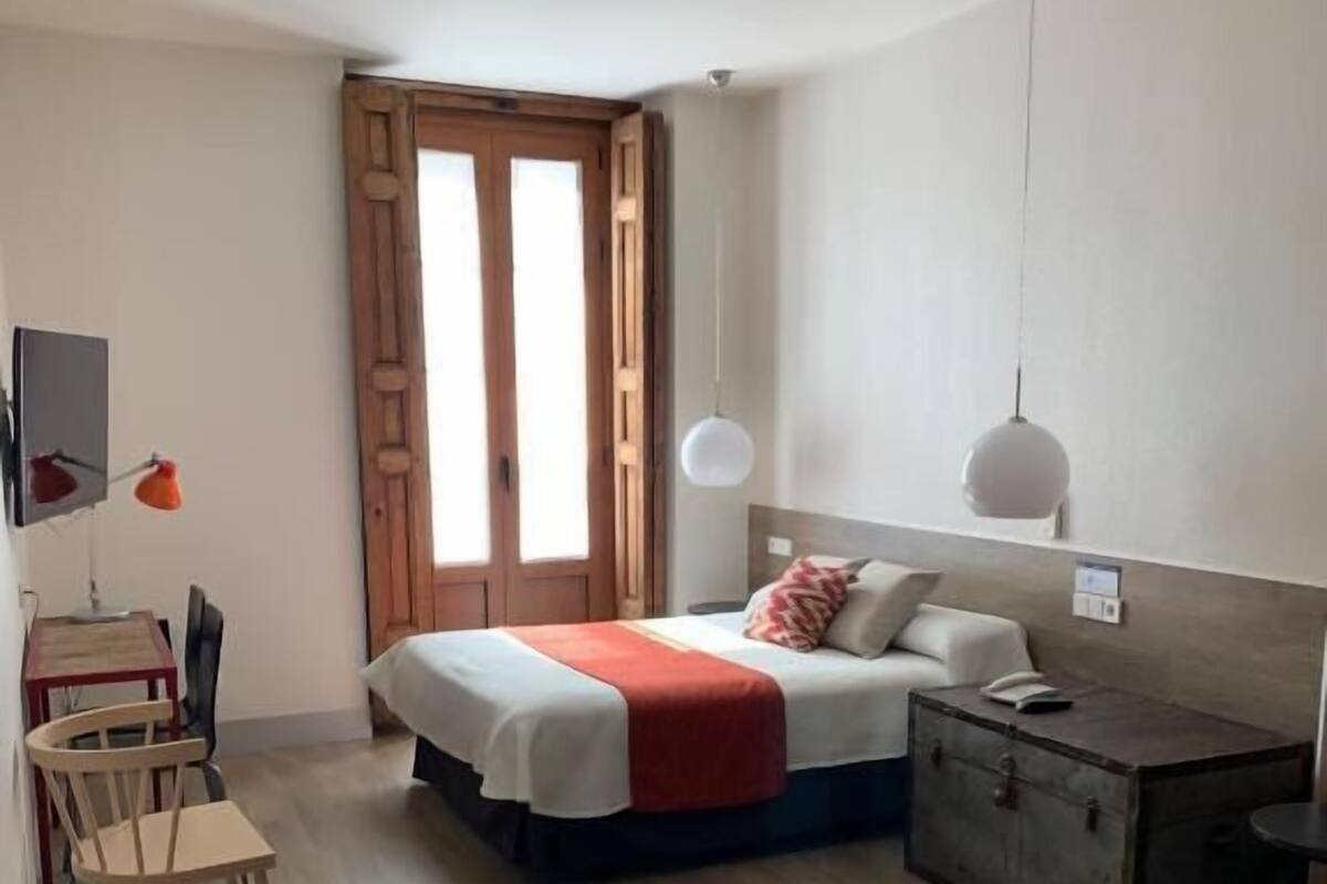Um quarto com cama, mesa de cabeceira, abajur e um baú de madeira.