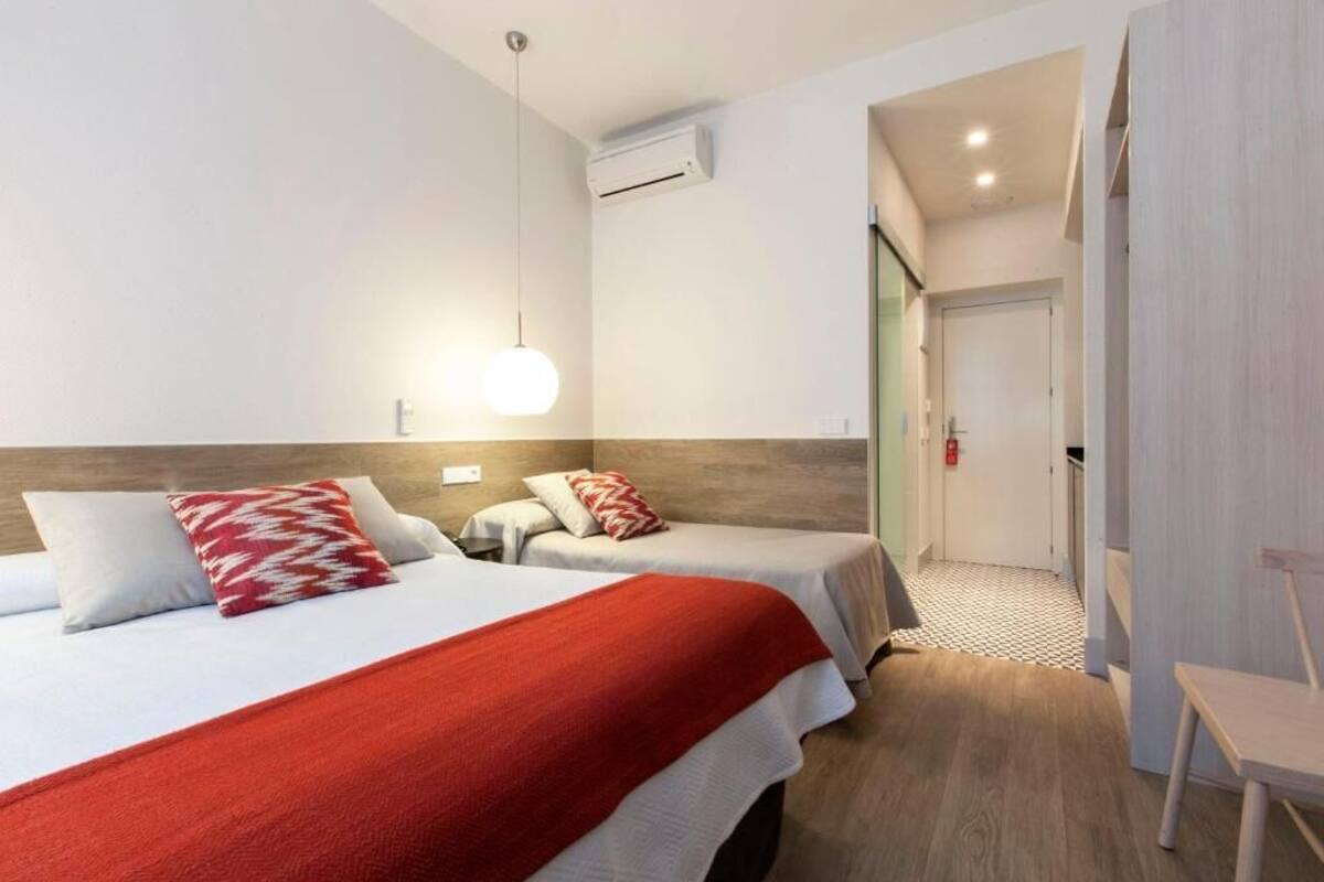 Quarto de hotel com duas camas, um cobertor vermelho, um travesseiro branco, uma cabeceira de madeira e uma luminária no teto.