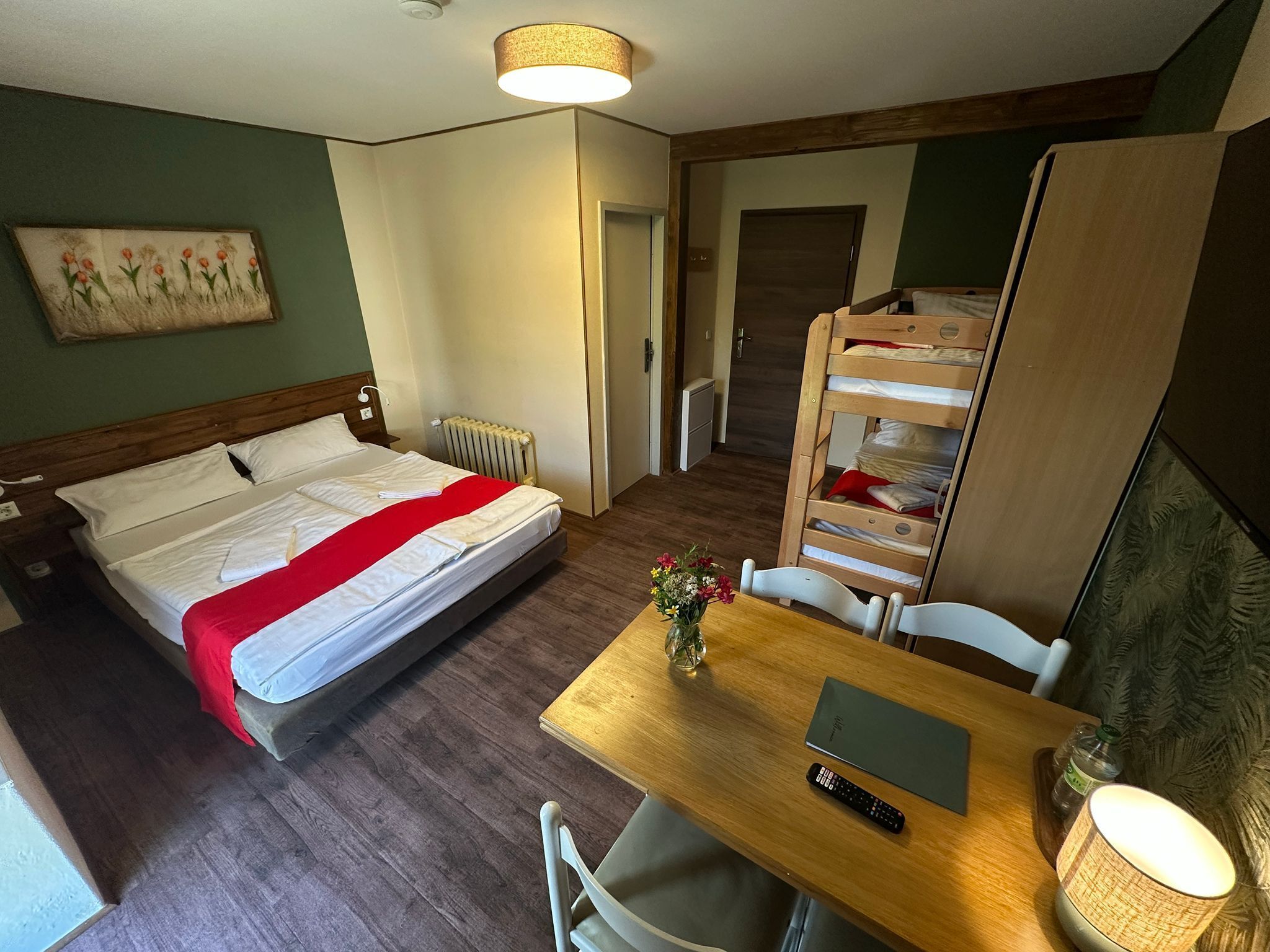 Quarto com uma cama, escrivaninha com cadeira, beliche, radiador e um quadro na parede.