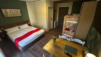 Quarto com uma cama, escrivaninha com cadeira, beliche, radiador e um quadro na parede.