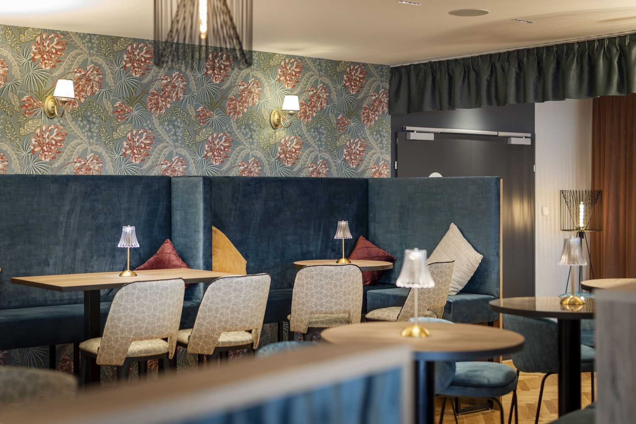 Um restaurante acolhedor com assentos estofados em azul, papel de parede estampado e iluminação ambiente.
