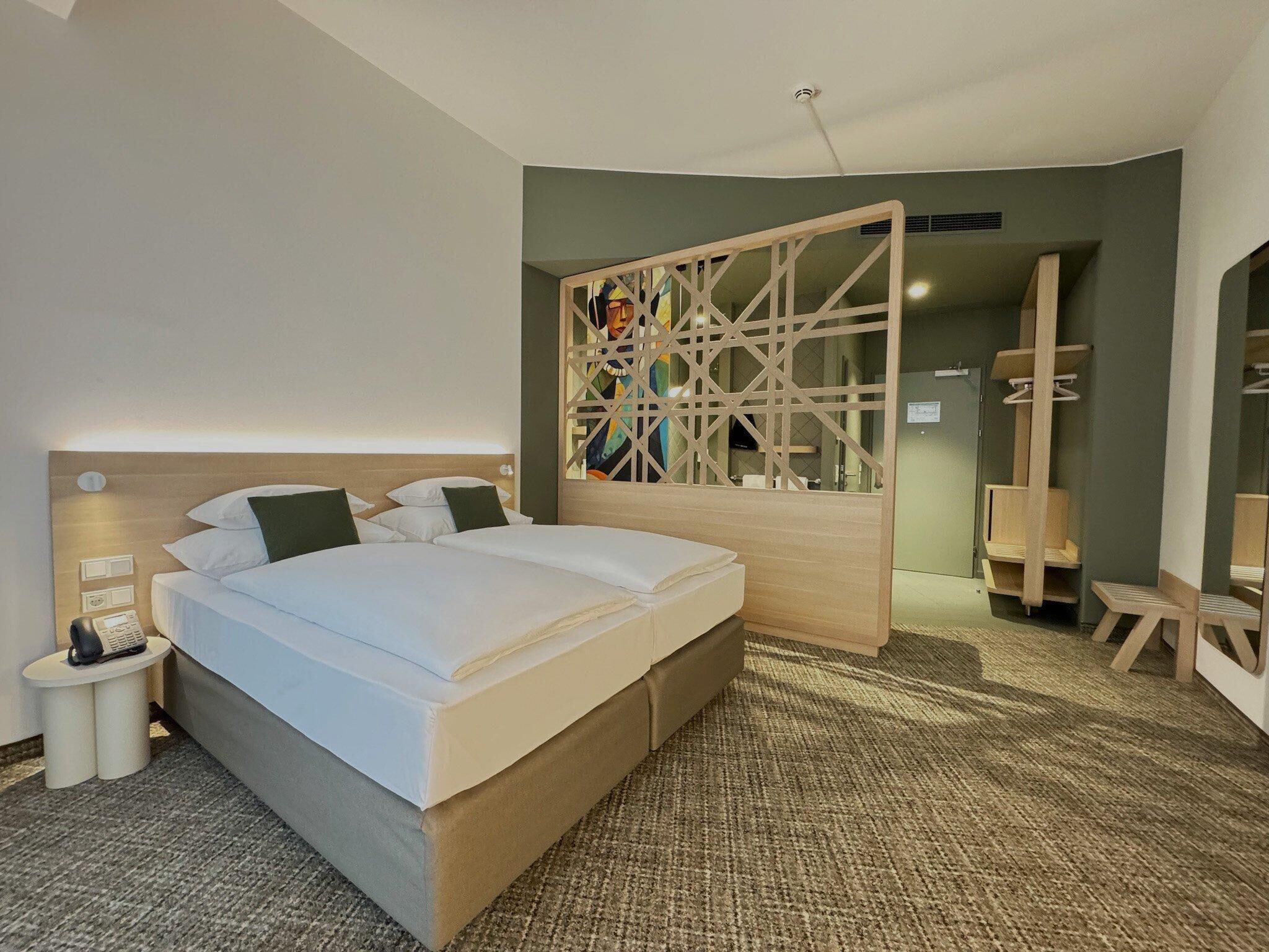 Quarto de hotel moderno com uma cama grande, telefone ao lado da cama e uma mesinha.