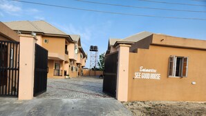 Uma entrada gradeada para uma área residencial, com uma placa que diz 'Enimarite SEE GOOD HOUSE'.