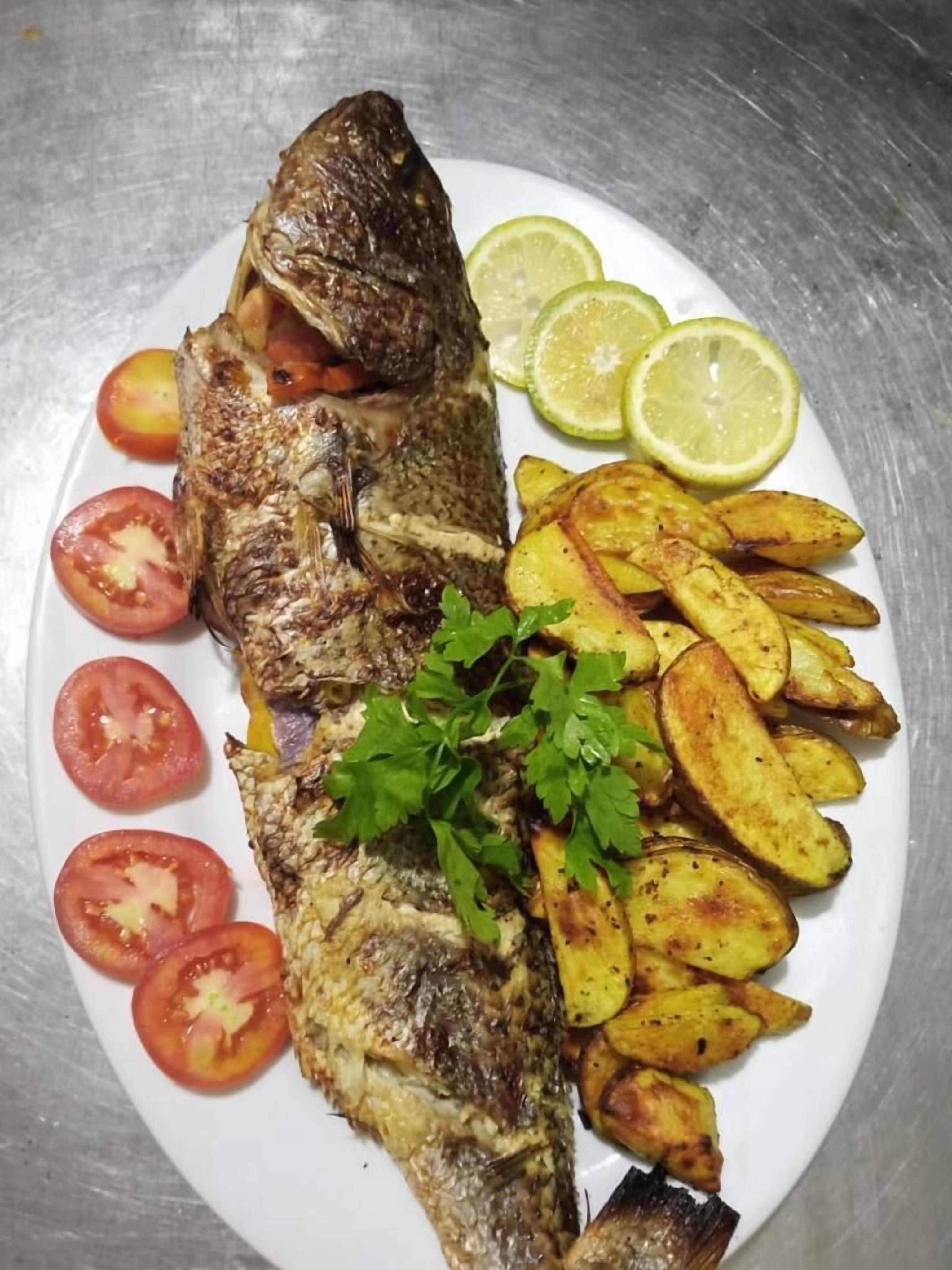 Um prato com peixe grelhado, tomates fatiados, gomos de limão e batatas assadas.