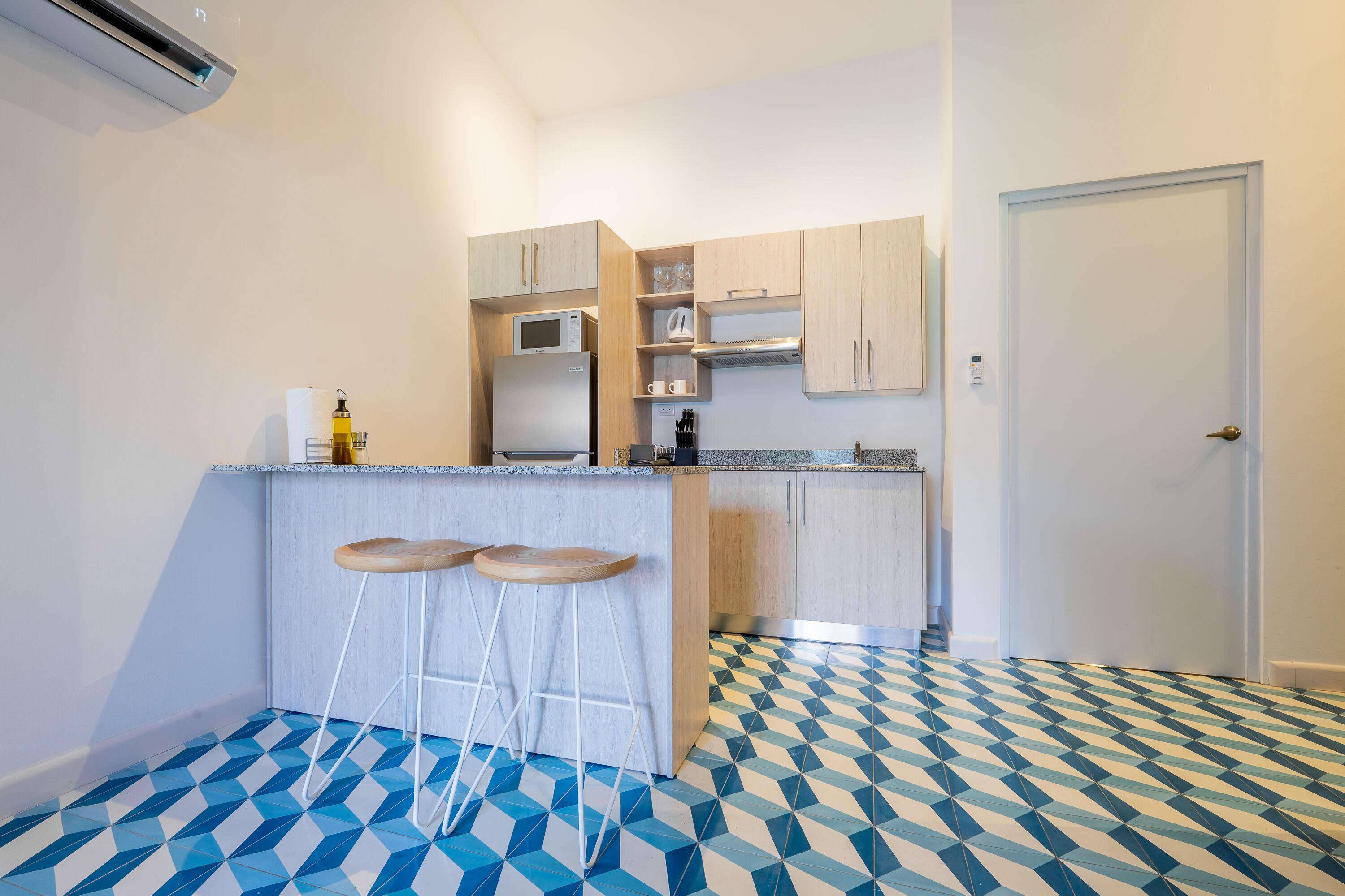Uma cozinha compacta com bancada, dois bancos e piso estampado.