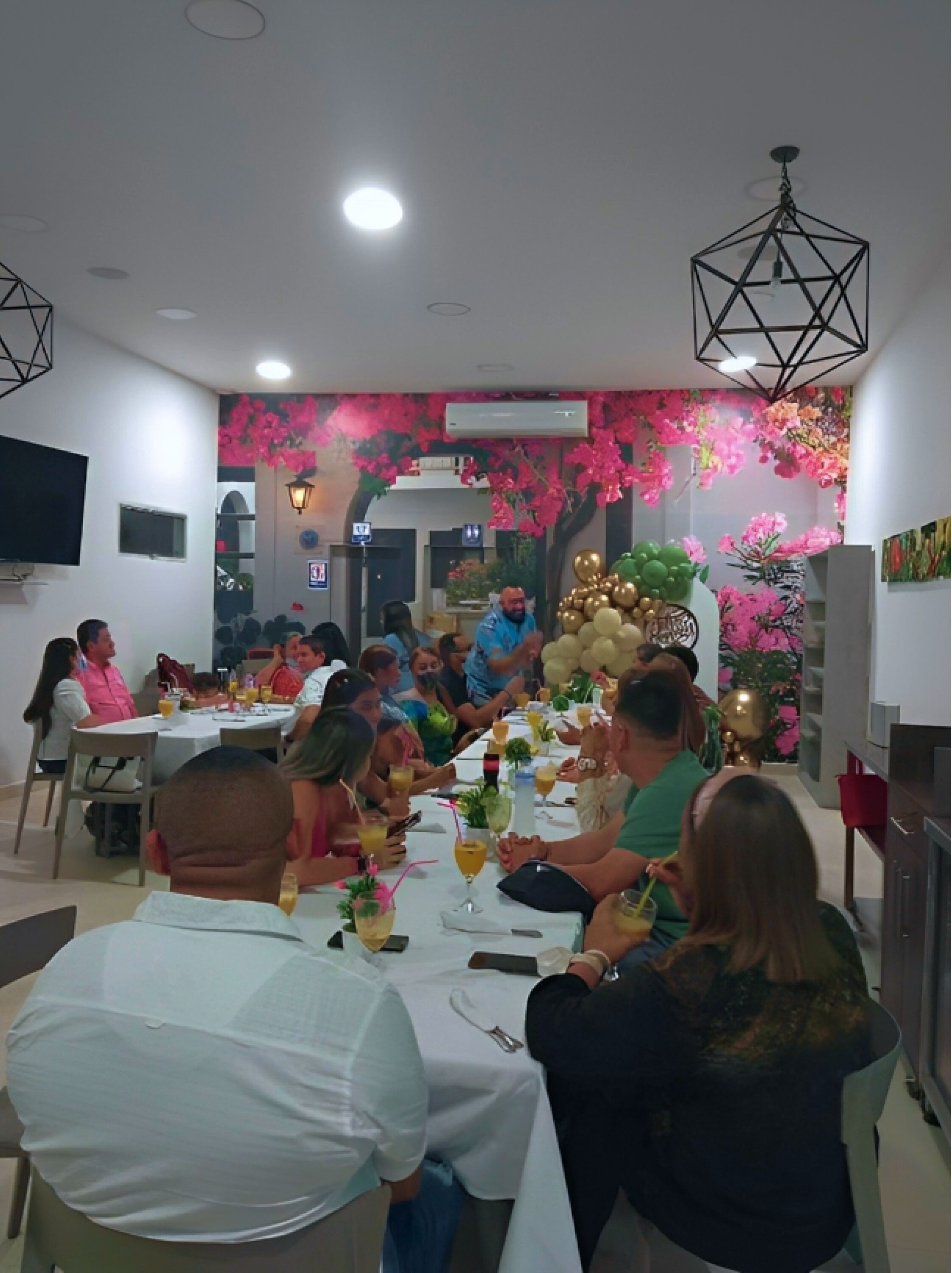 Uma sala de jantar com mesas redondas, hóspedes sentados e uma parede decorativa com motivos florais.