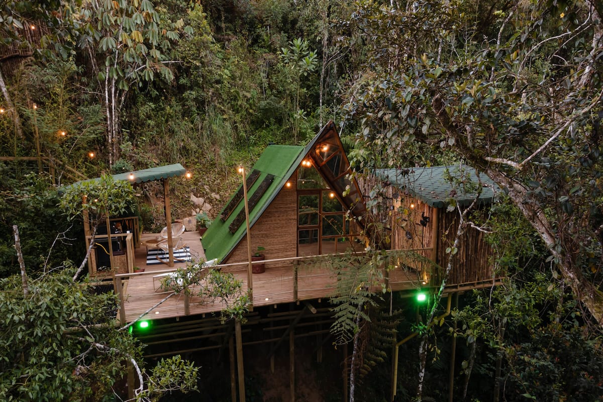 Uma casa na árvore com um deck de madeira, telhado verde e luzes de cordão.