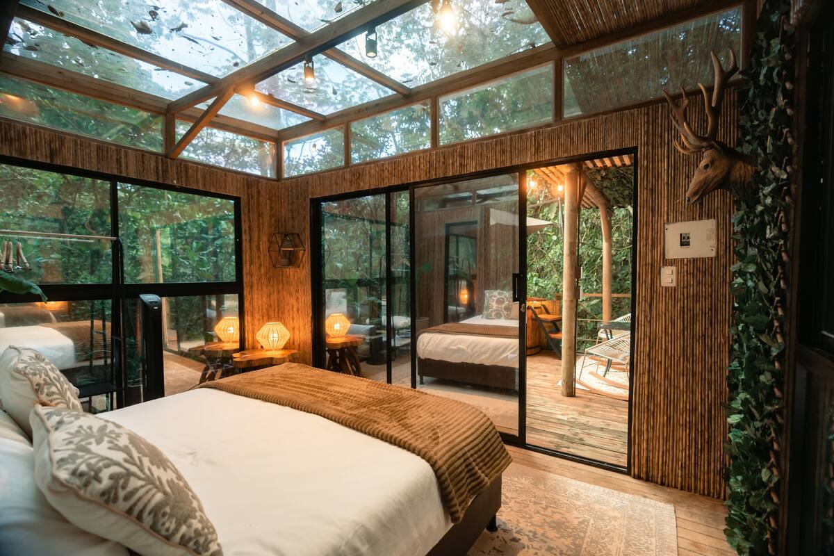 Quarto espaçoso com uma cama grande, porta de vidro que dá para uma varanda e teto de madeira.
