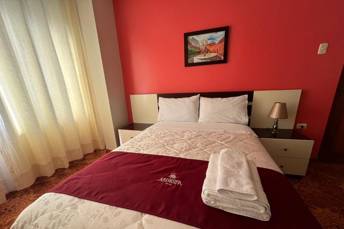 Quarto de hotel com uma cama, uma mesa de cabeceira, uma luminária e um quadro na parede.