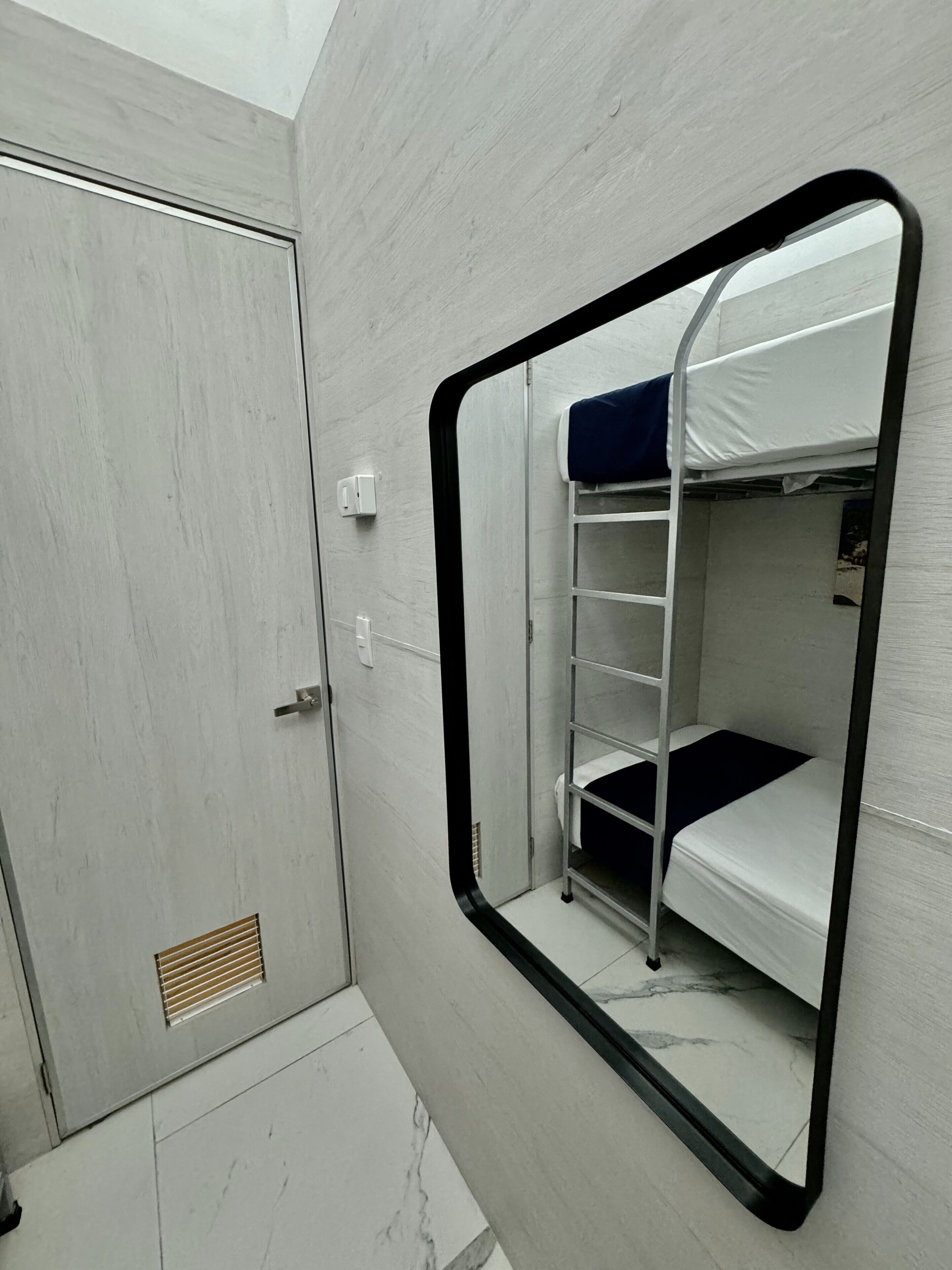 Quarto com beliche, porta branca, pequena janela com persianas e chão ladrilhado.