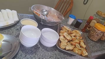 Uma bancada de cozinha com diversos alimentos e recipientes, incluindo um prato de pão, tigelas de creme e potes de especiarias.