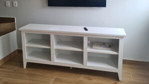 Um móvel branco para TV com prateleiras, uma televisão de tela plana na parede e um chão de madeira.