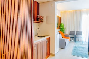 Cozinha moderna com pia e armários, área de refeições com sofá e cadeiras, e sala de estar com um sofá e uma planta.