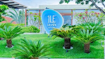 Placa de hotel com a inscrição 'ILE DEPIPA RESORT', rodeada por vegetação exuberante e palmeiras.