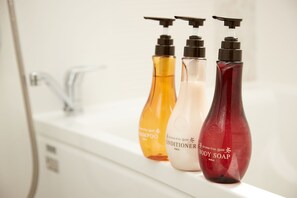 Três frascos de shampoo, condicionador e sabonete líquido em uma prateleira branca.