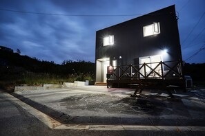 Um edifício moderno de dois andares com telhado plano, um pequeno alpendre e entrada visível.
